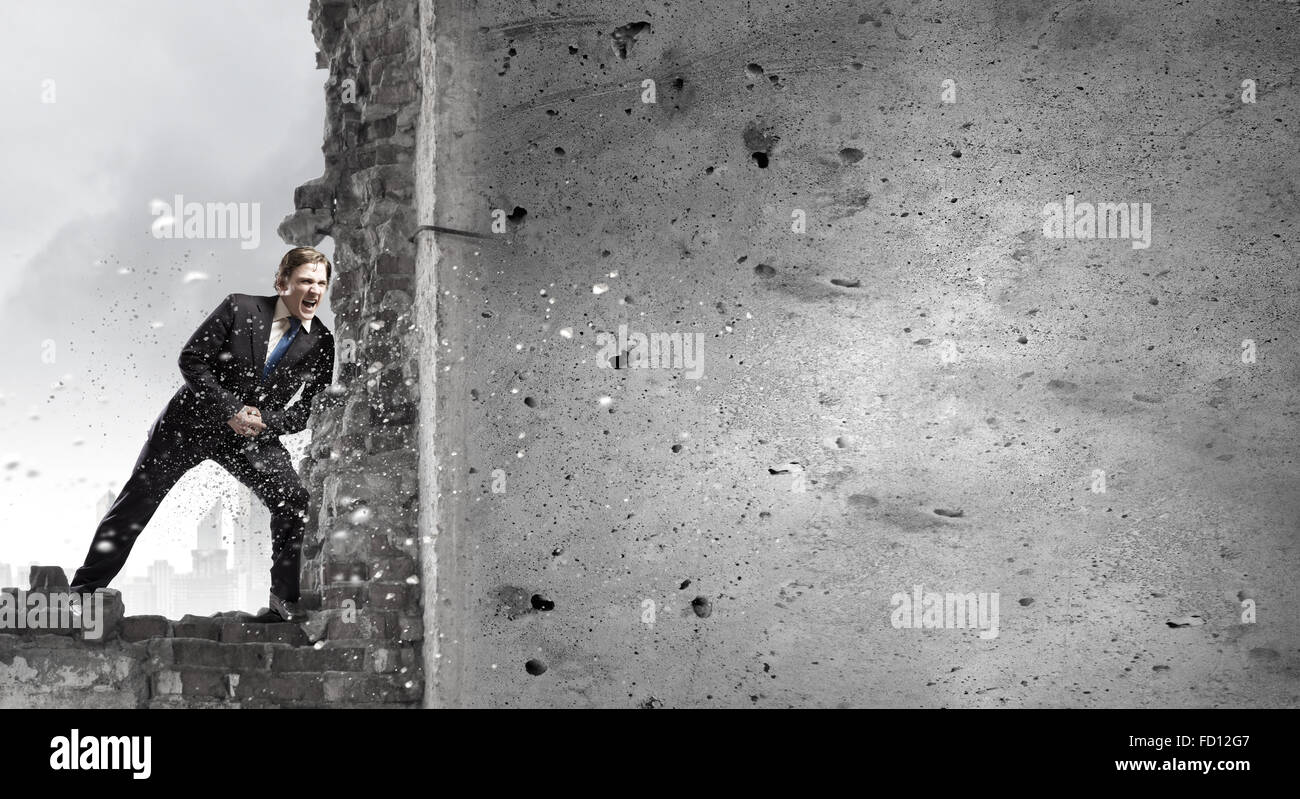 Young businessman making effort to move stone wall Stock Photo - Alamy