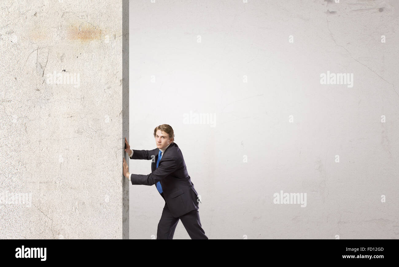 Young businessman making effort to move stone wall Stock Photo - Alamy