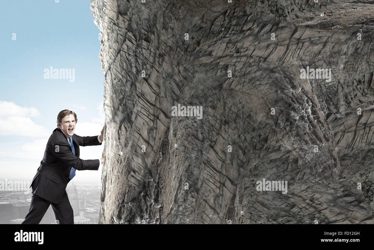 Young businessman making effort to move stone wall Stock Photo - Alamy