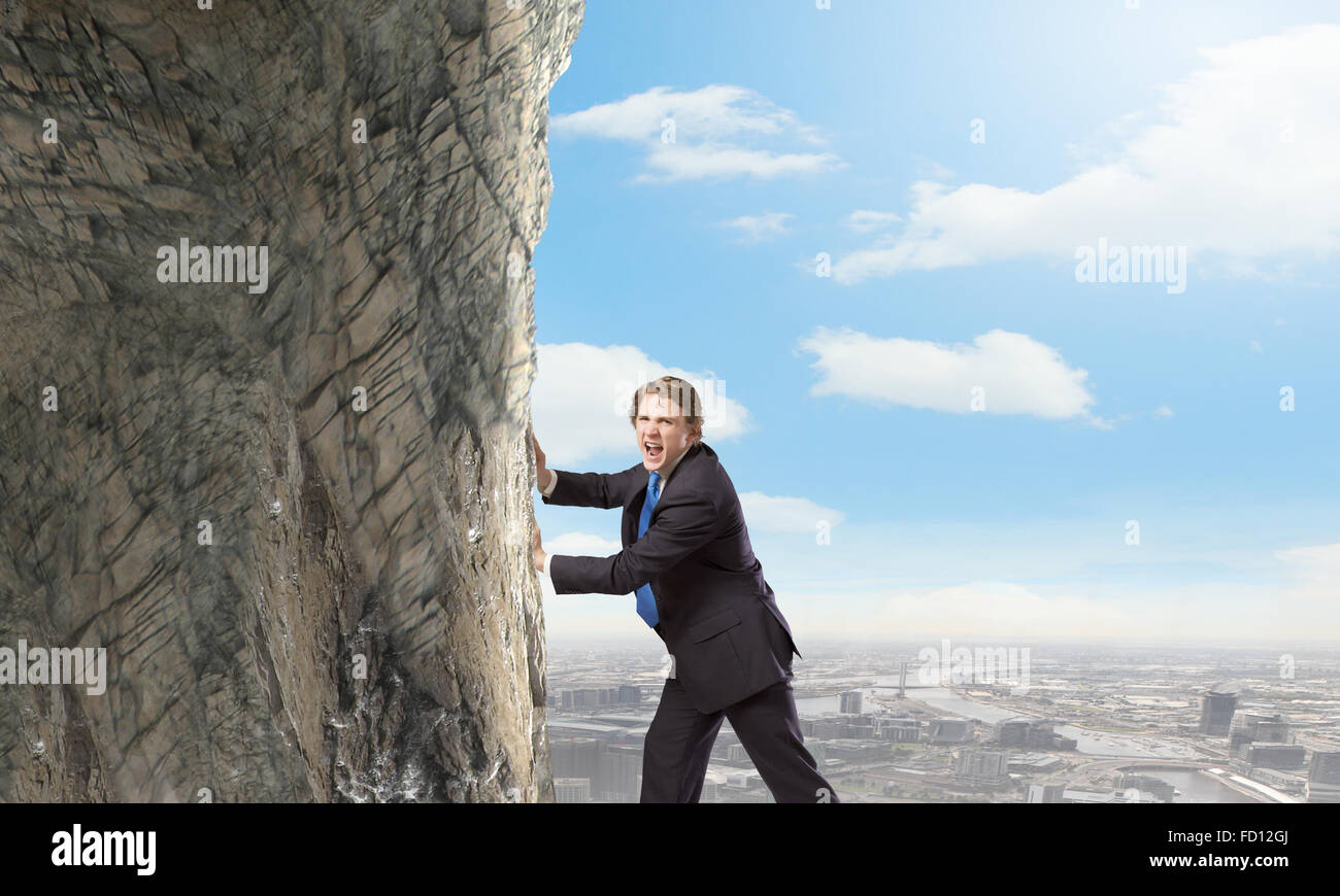 Young businessman making effort to move stone wall Stock Photo - Alamy