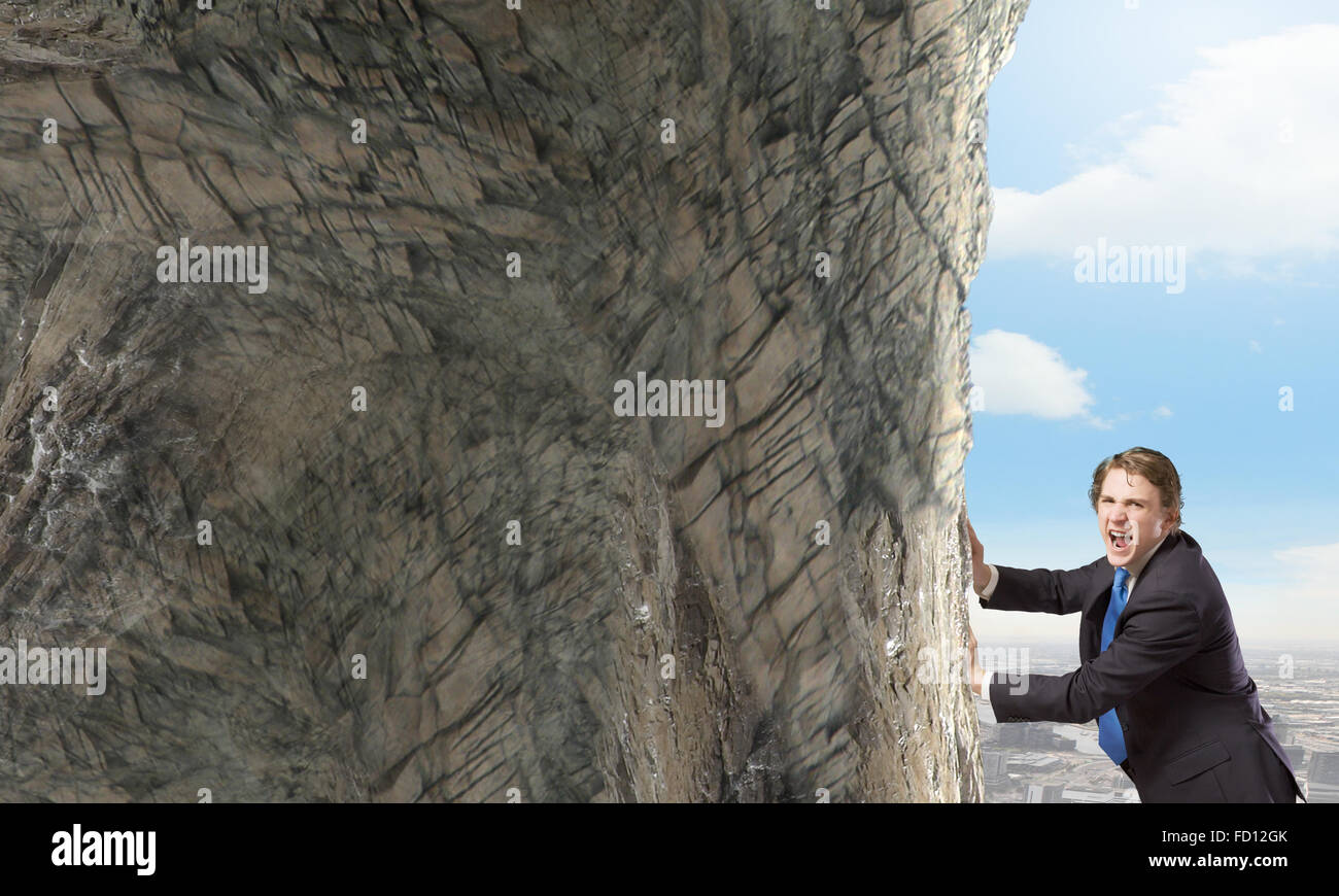 Young businessman making effort to move stone wall Stock Photo - Alamy