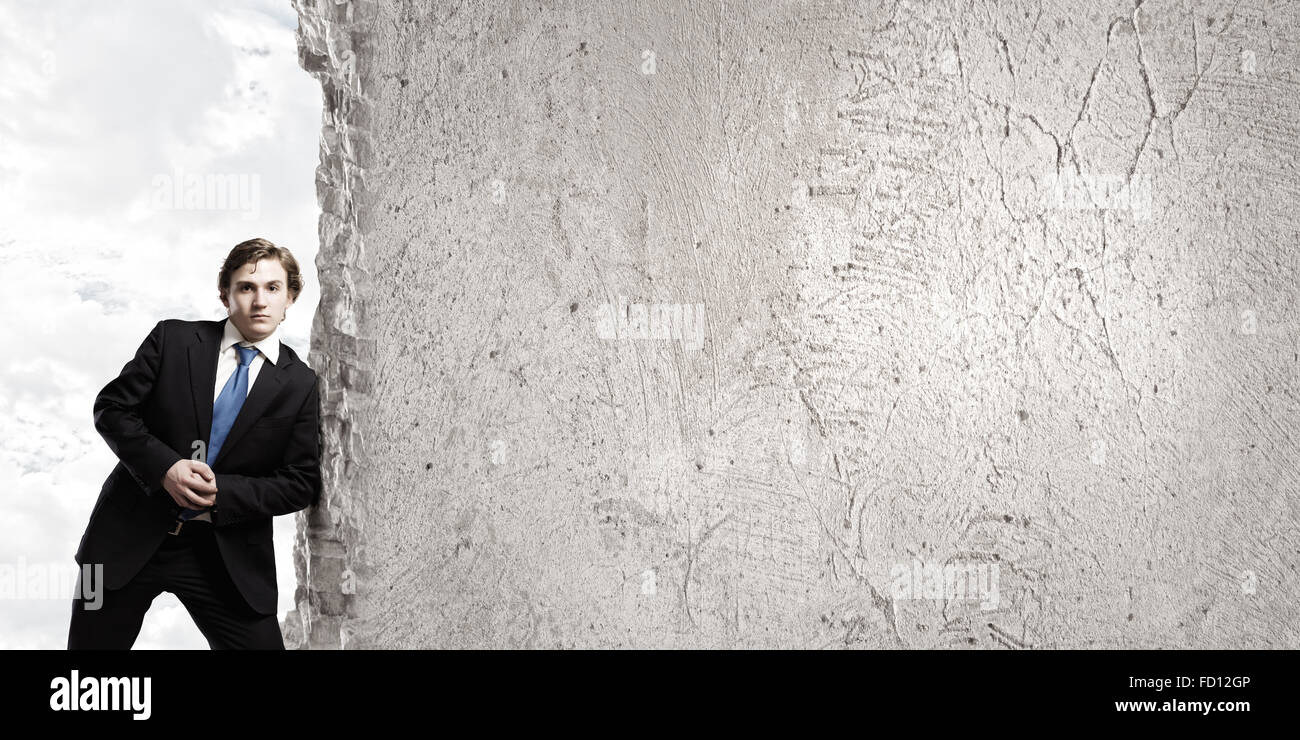 Young businessman making effort to move stone wall Stock Photo - Alamy