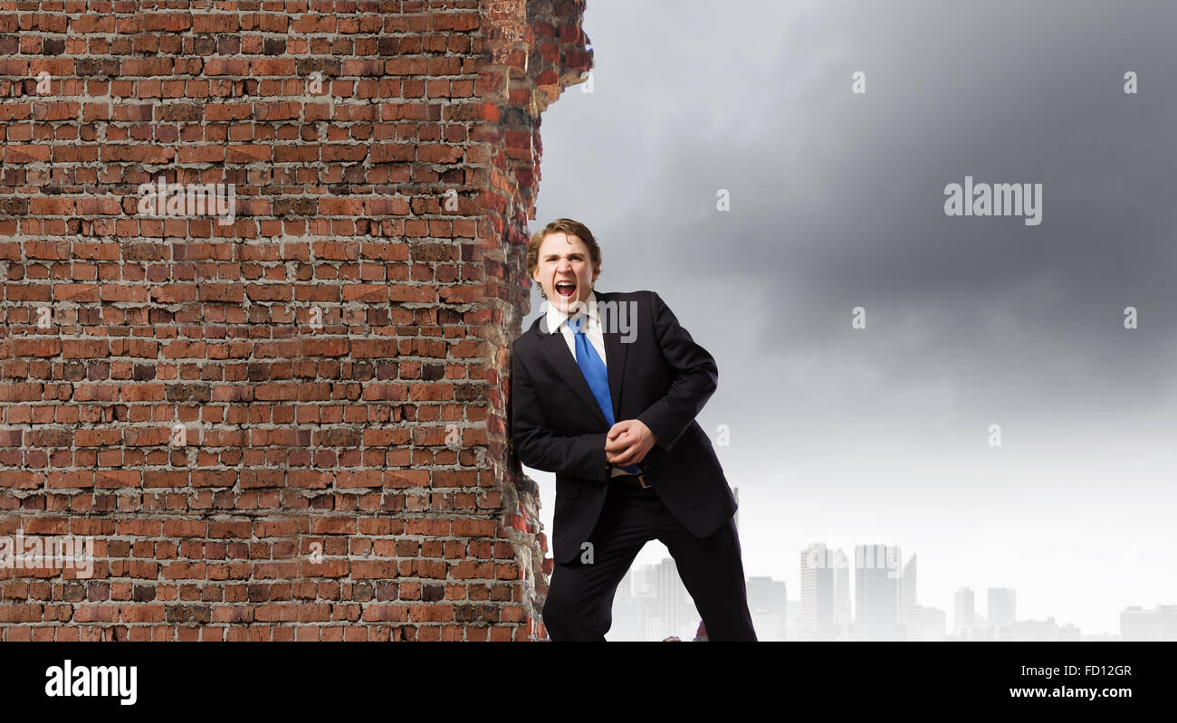 Young businessman making effort to move brick wall Stock Photo - Alamy