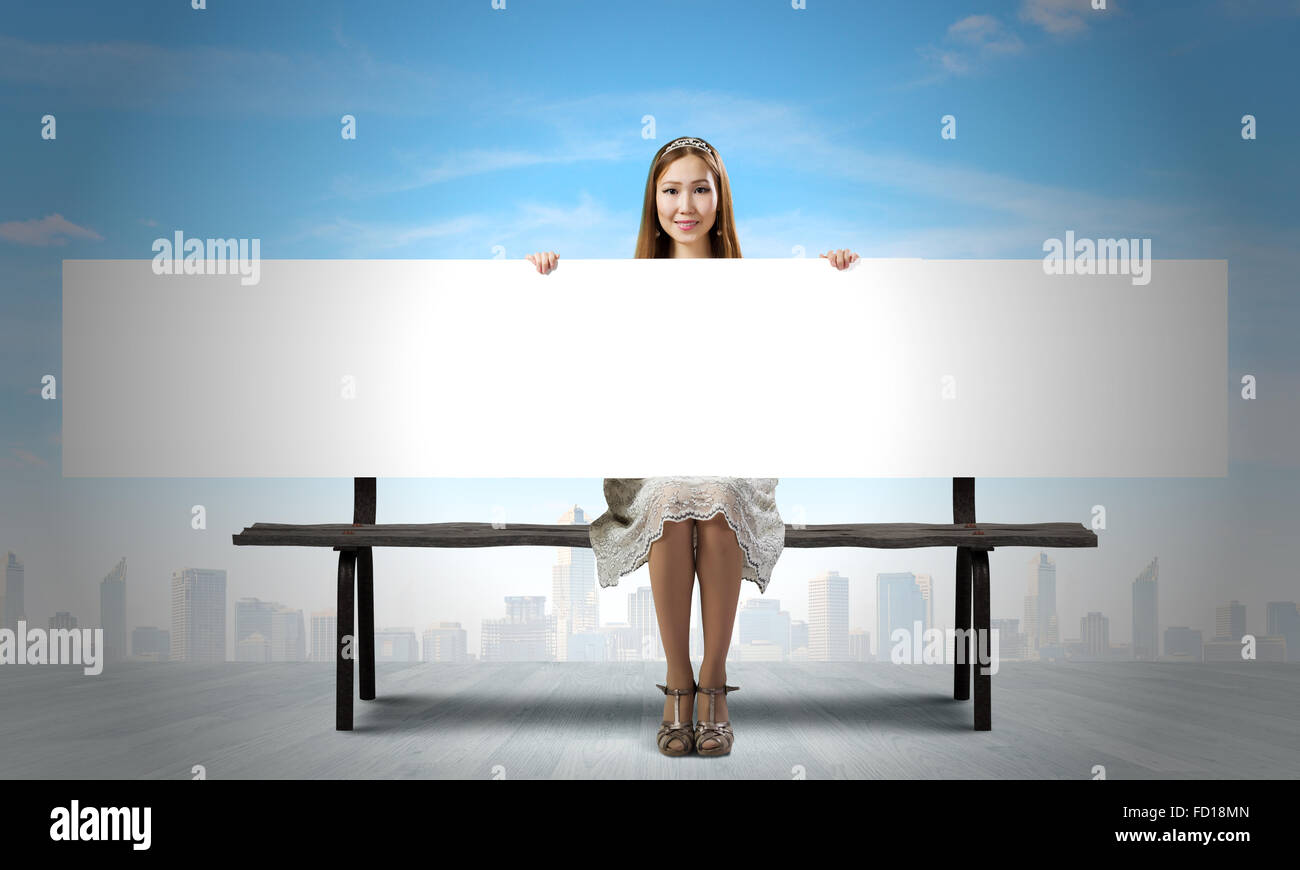 Young asian woman sitting on bench with blank banner Stock Photo - Alamy