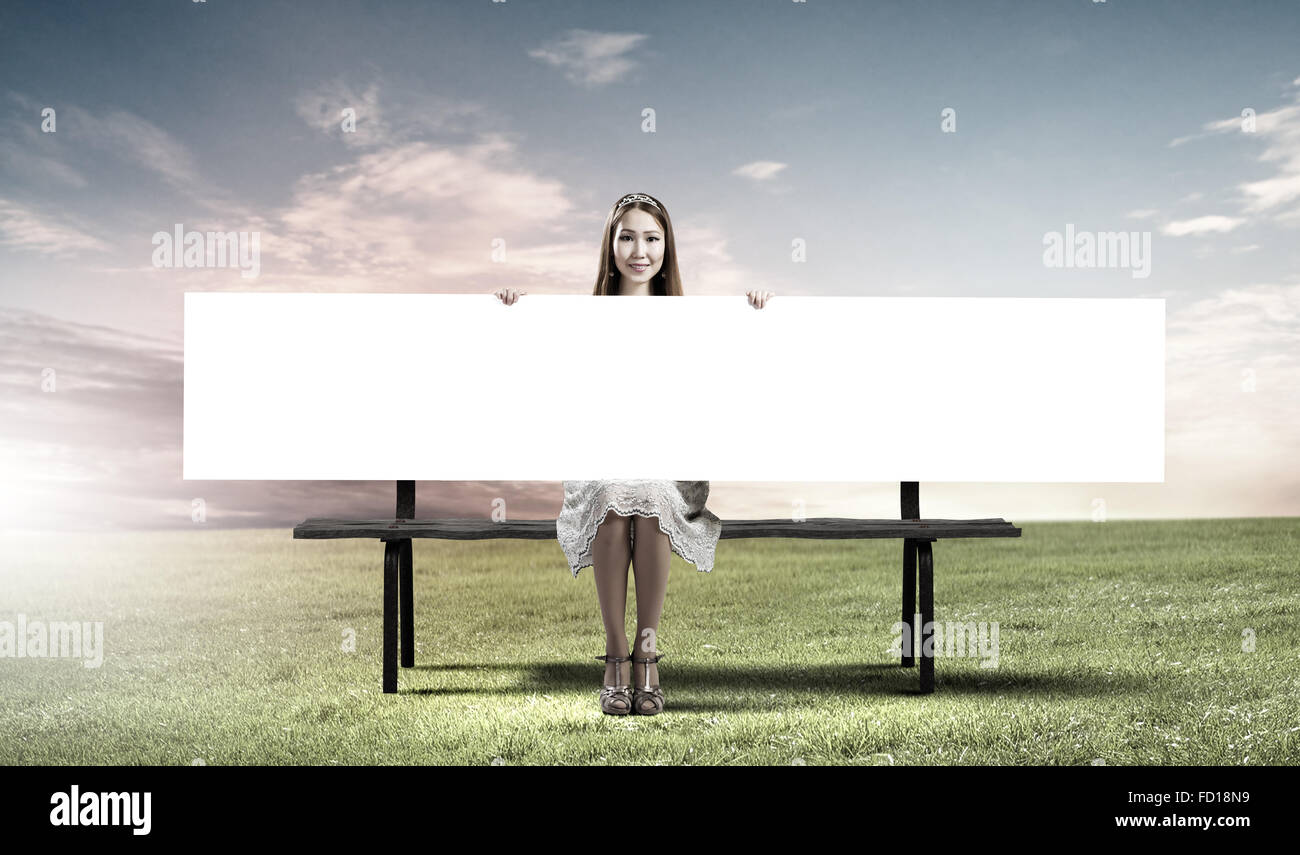 Young asian woman sitting on bench with blank banner Stock Photo - Alamy