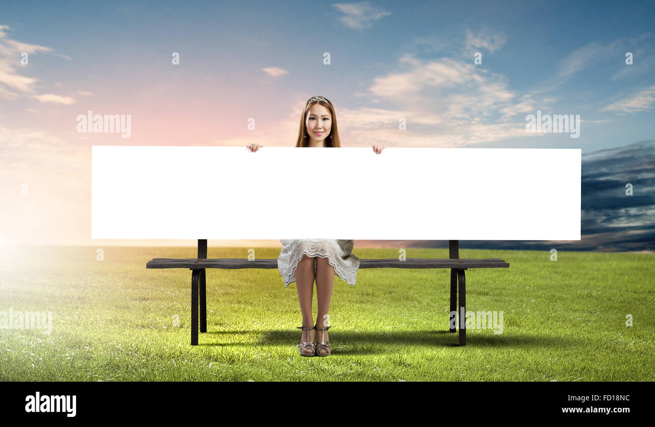 Young asian woman sitting on bench with blank banner Stock Photo - Alamy