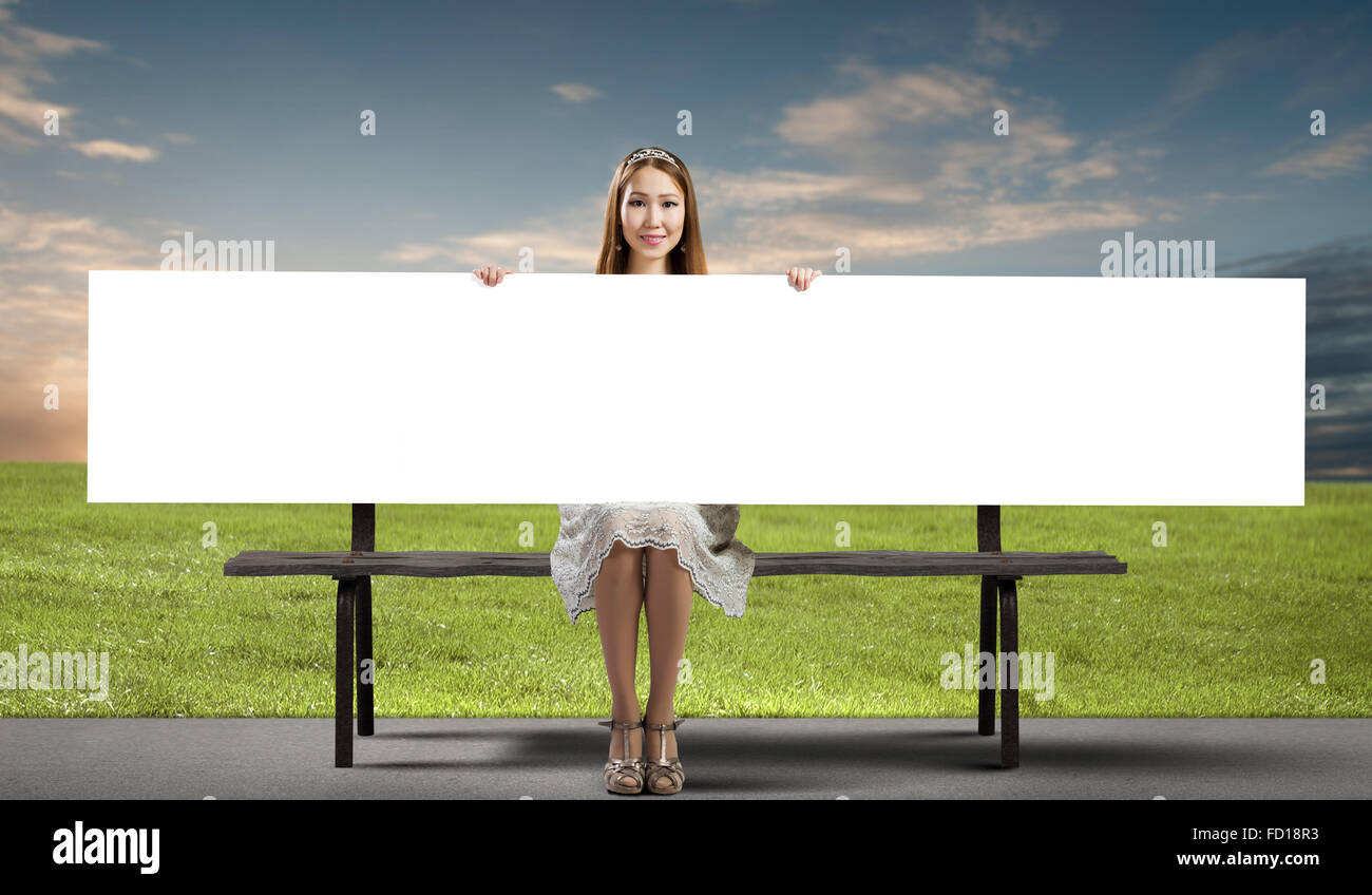 Young asian woman sitting on bench with blank banner Stock Photo - Alamy