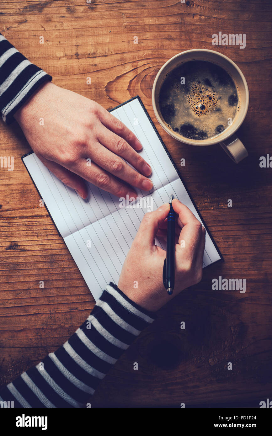 Woman drinking coffee and making a diary note, top view of female hands ...