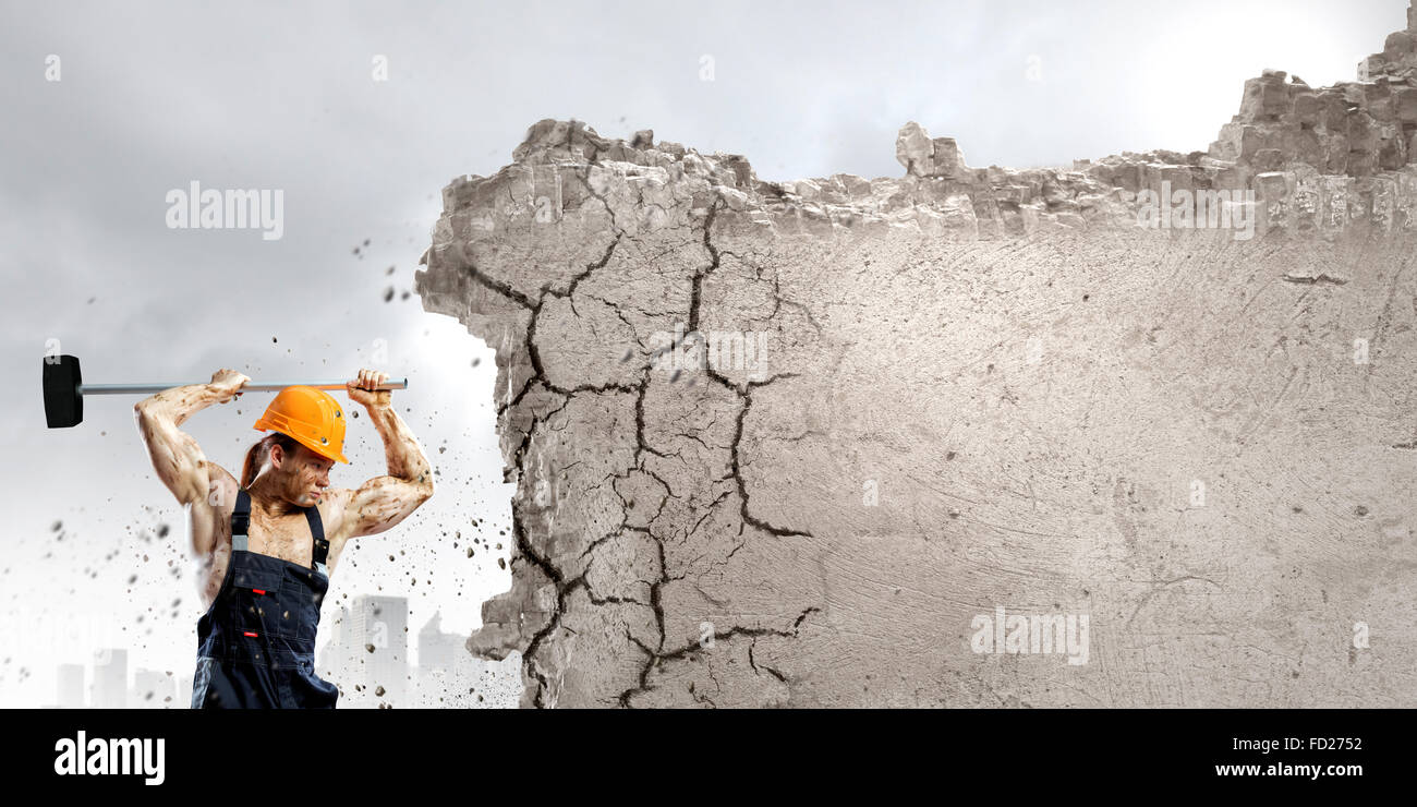 Strong man in uniform breaking wall with hammer Stock Photo - Alamy