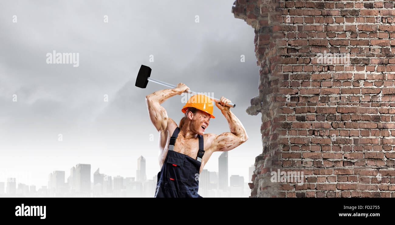 Strong man in uniform breaking brick wall with hammer Stock Photo - Alamy