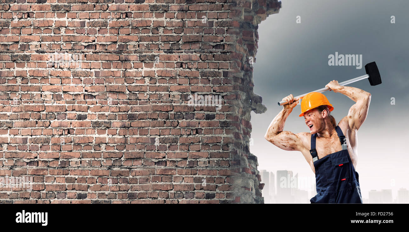 Strong man in uniform breaking brick wall with hammer Stock Photo - Alamy