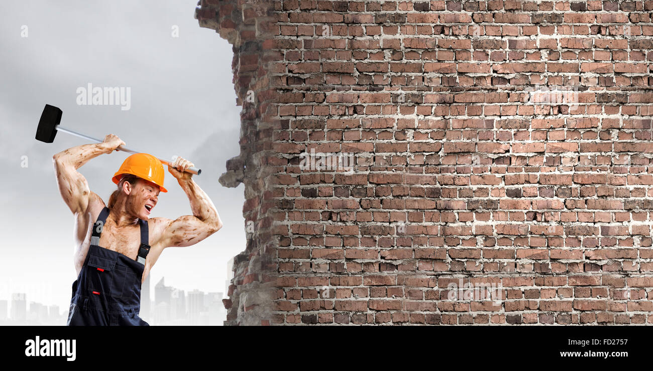Strong man in uniform breaking brick wall with hammer Stock Photo - Alamy