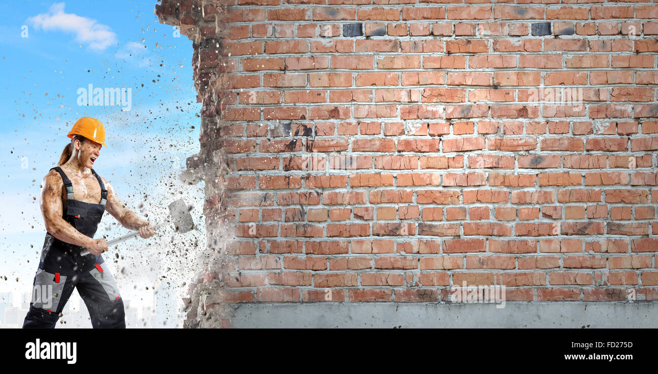 Strong man in uniform breaking brick wall with hammer Stock Photo - Alamy