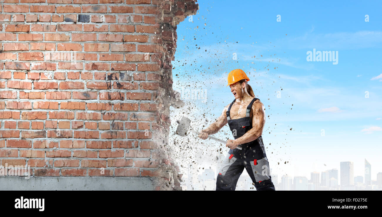 Strong man in uniform breaking brick wall with hammer Stock Photo - Alamy