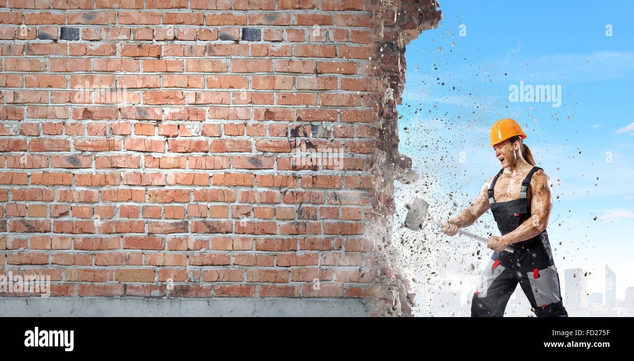Strong man in uniform breaking brick wall with hammer Stock Photo - Alamy