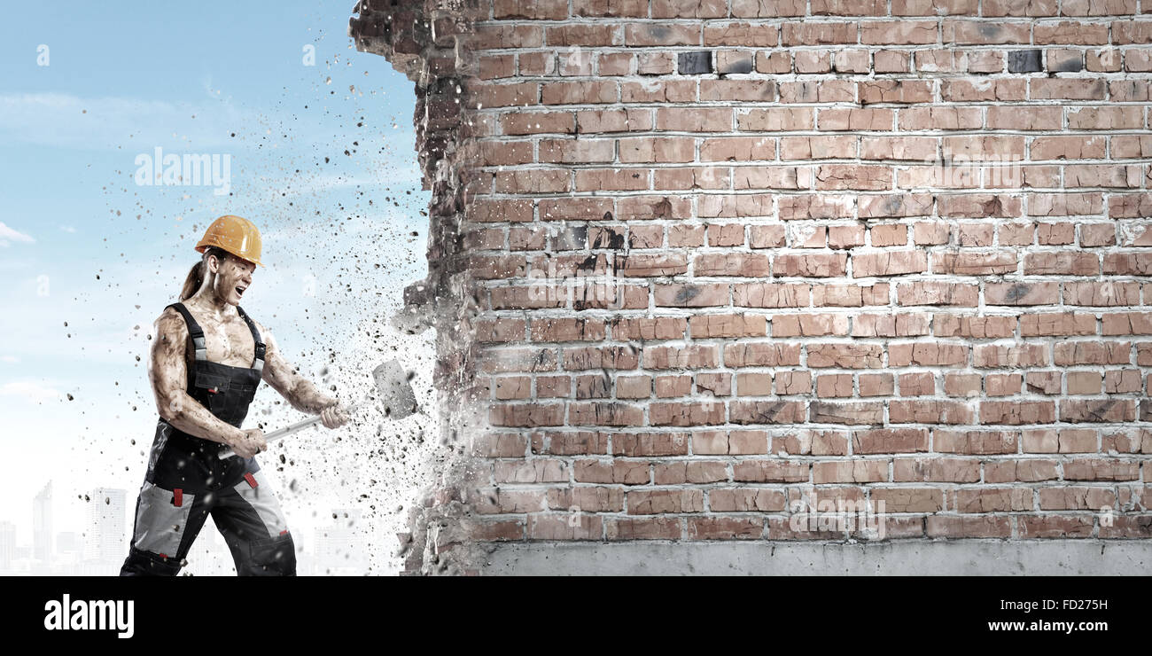 Strong man in uniform breaking brick wall with hammer Stock Photo - Alamy