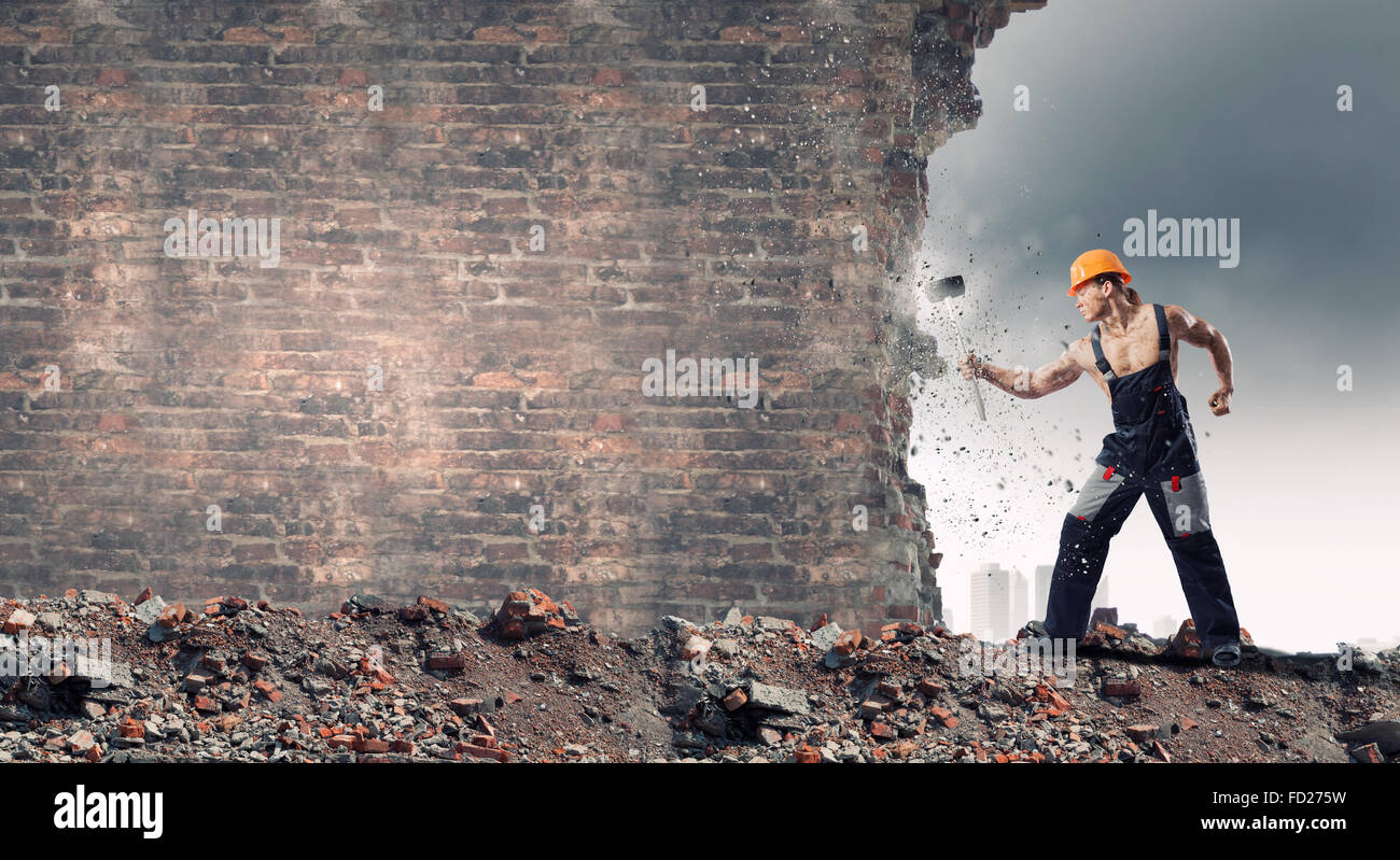 Strong man in uniform breaking brick wall with hammer Stock Photo - Alamy