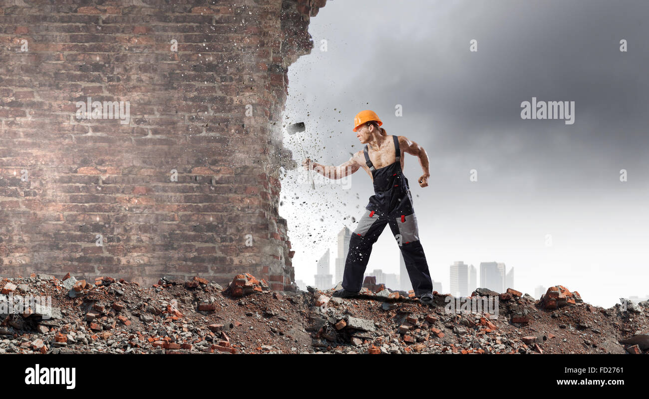 Strong man in uniform breaking brick wall with hammer Stock Photo - Alamy