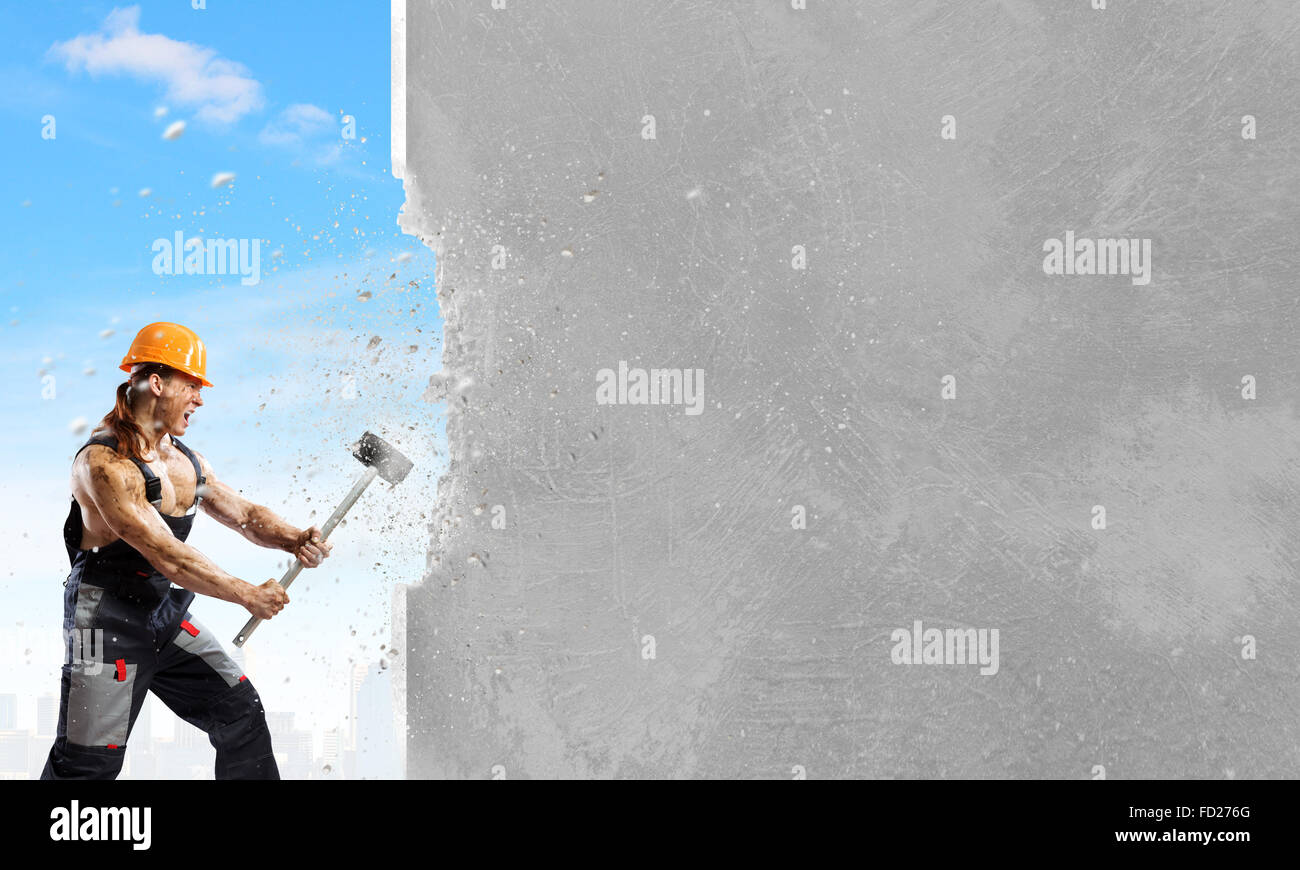 Strong man in uniform breaking wall with hammer Stock Photo - Alamy