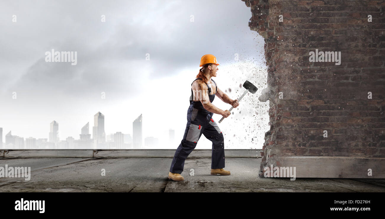 Strong man in uniform breaking brick wall with hammer Stock Photo - Alamy