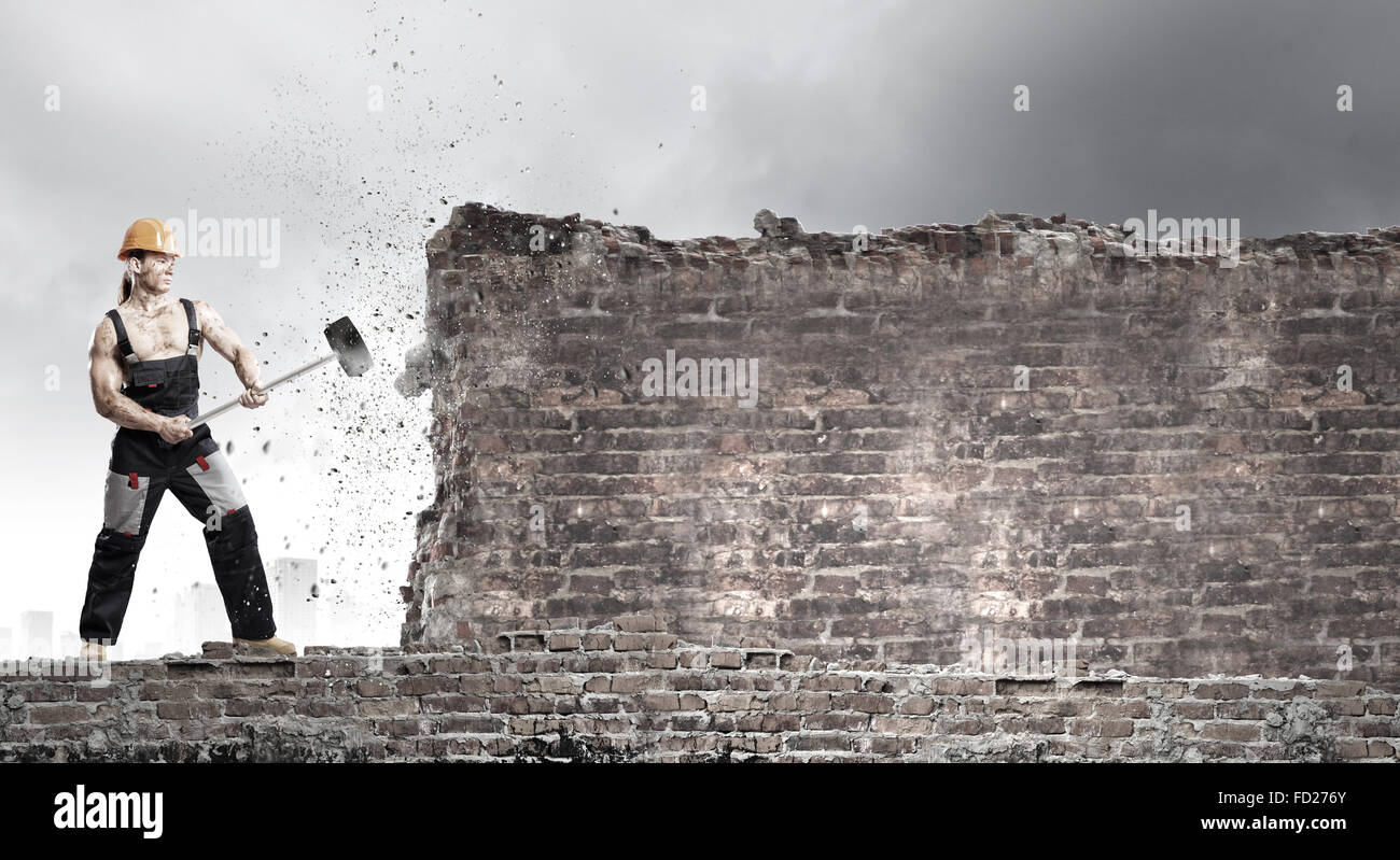 Strong man in uniform breaking brick wall with hammer Stock Photo - Alamy