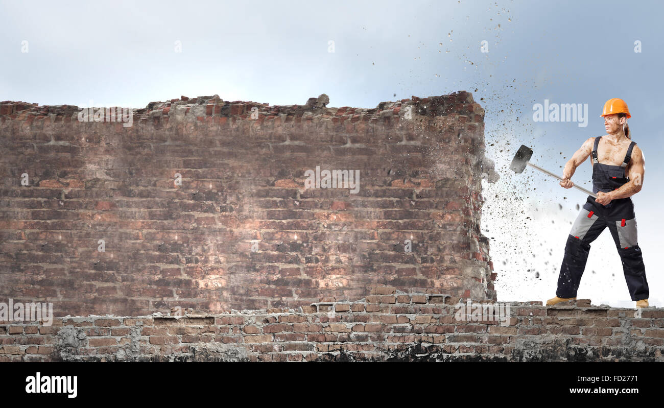 Strong man in uniform breaking brick wall with hammer Stock Photo - Alamy