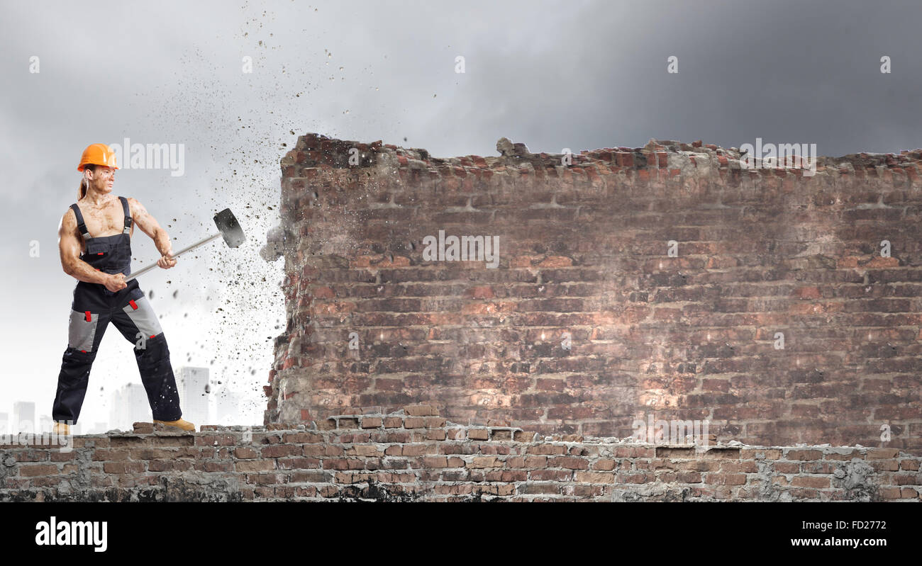 Strong man in uniform breaking brick wall with hammer Stock Photo - Alamy