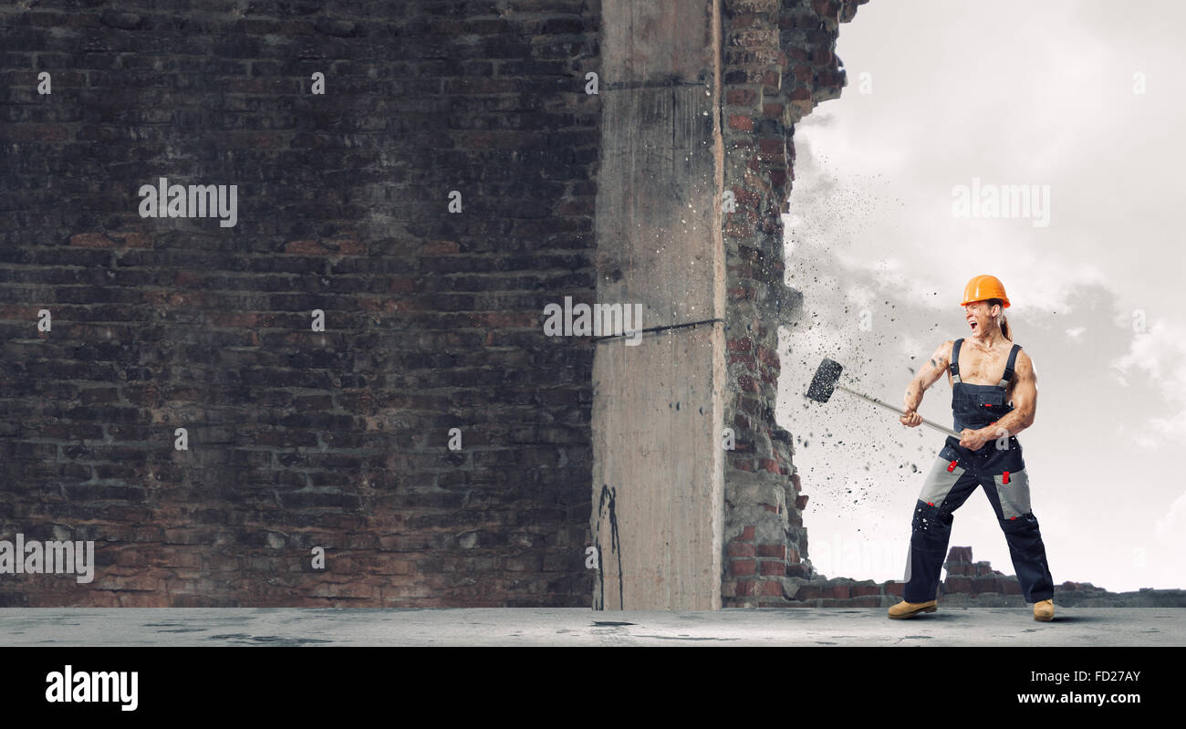Strong man in uniform breaking brick wall with hammer Stock Photo - Alamy
