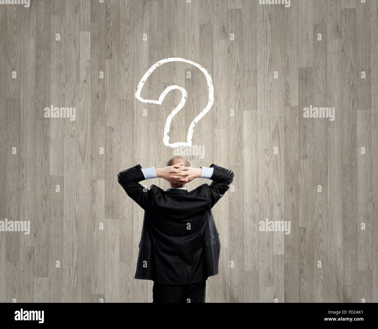 Rear view of businessman looking thoughtfully at question mark above ...