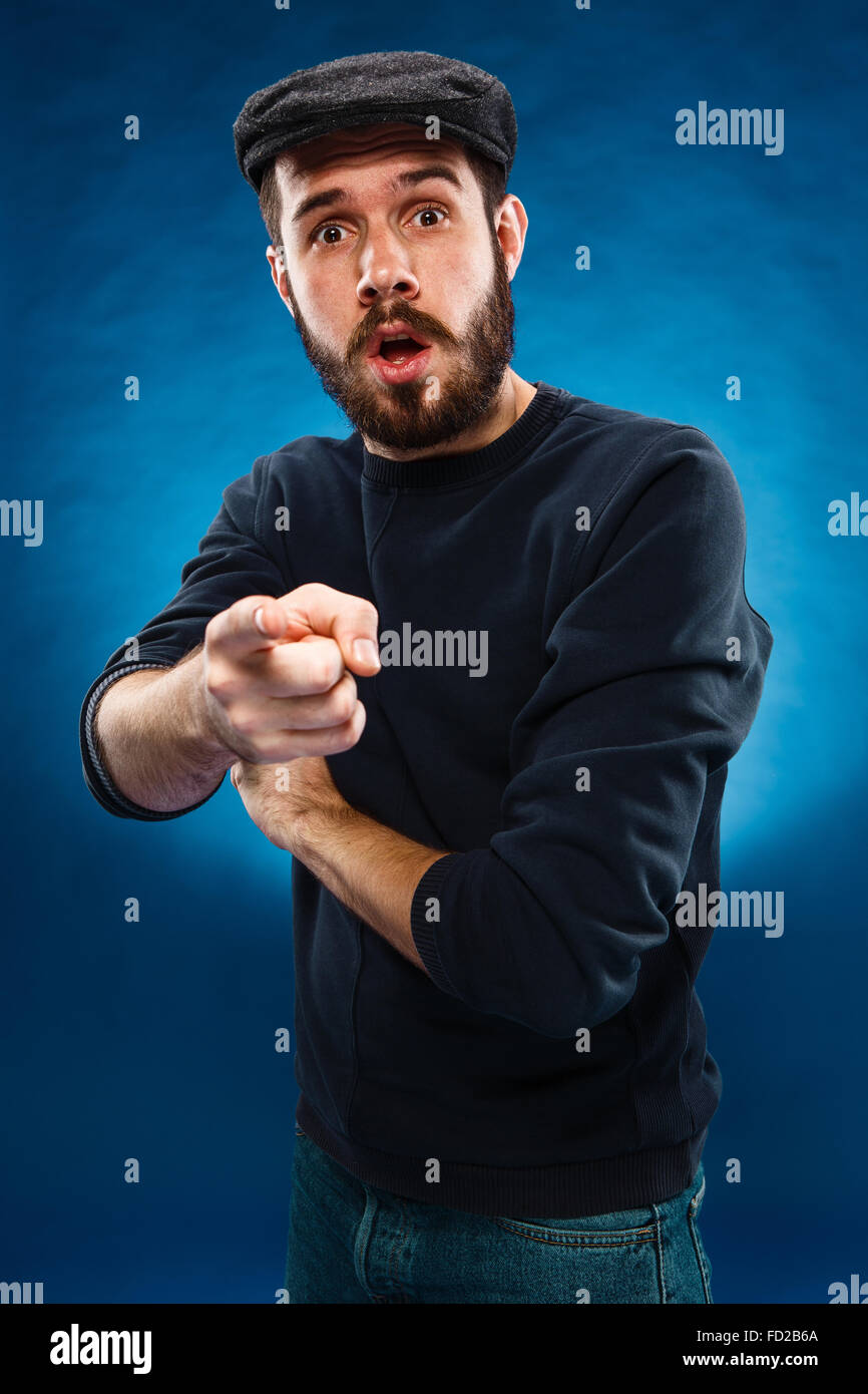 Young man in cap, finger pointing towards the camera on a blue ...