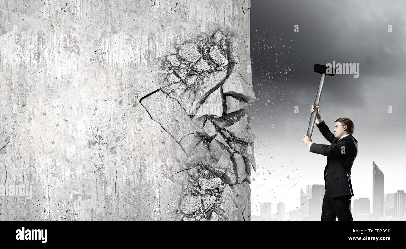 Young determined businessman crashing wall with hammer Stock Photo - Alamy