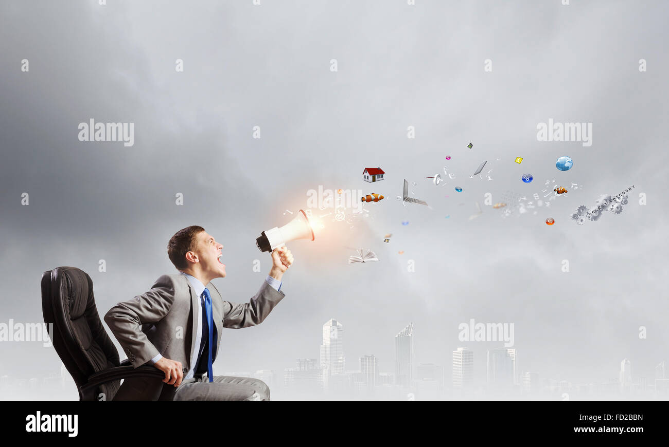 Young angry businessman sitting on chair and screaming in megaphone ...