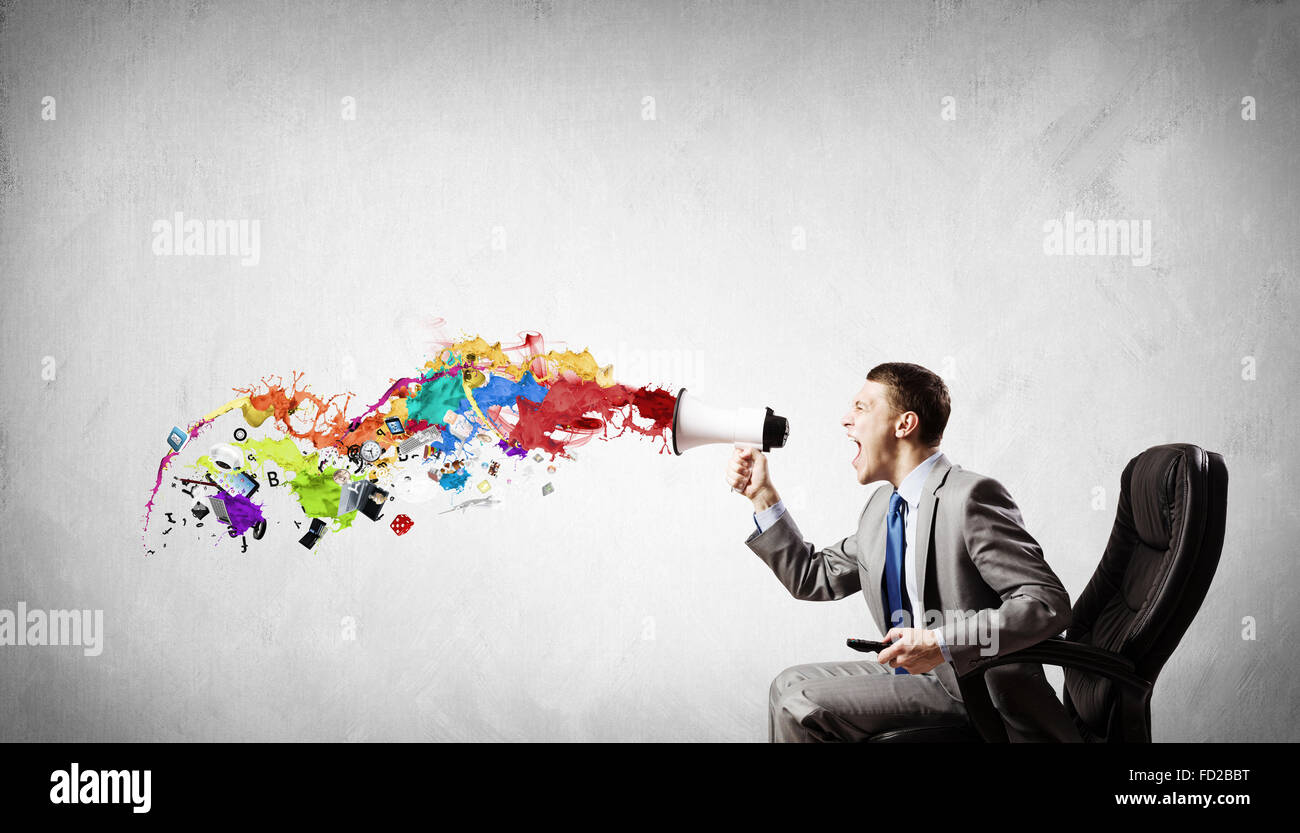 Young angry businessman sitting on chair and screaming in megaphone ...