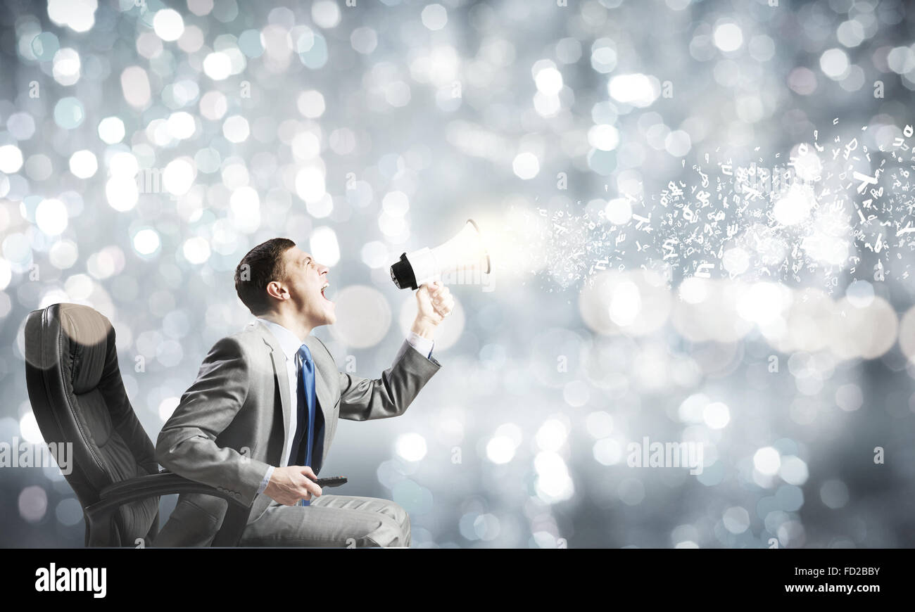 Young angry businessman sitting on chair and screaming in megaphone ...