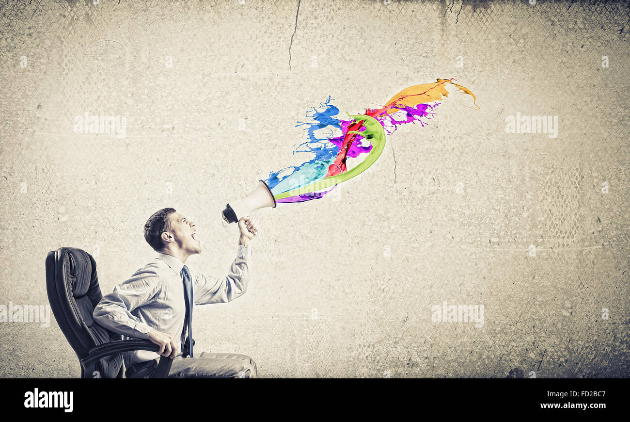 Young angry businessman sitting on chair and screaming in megaphone ...