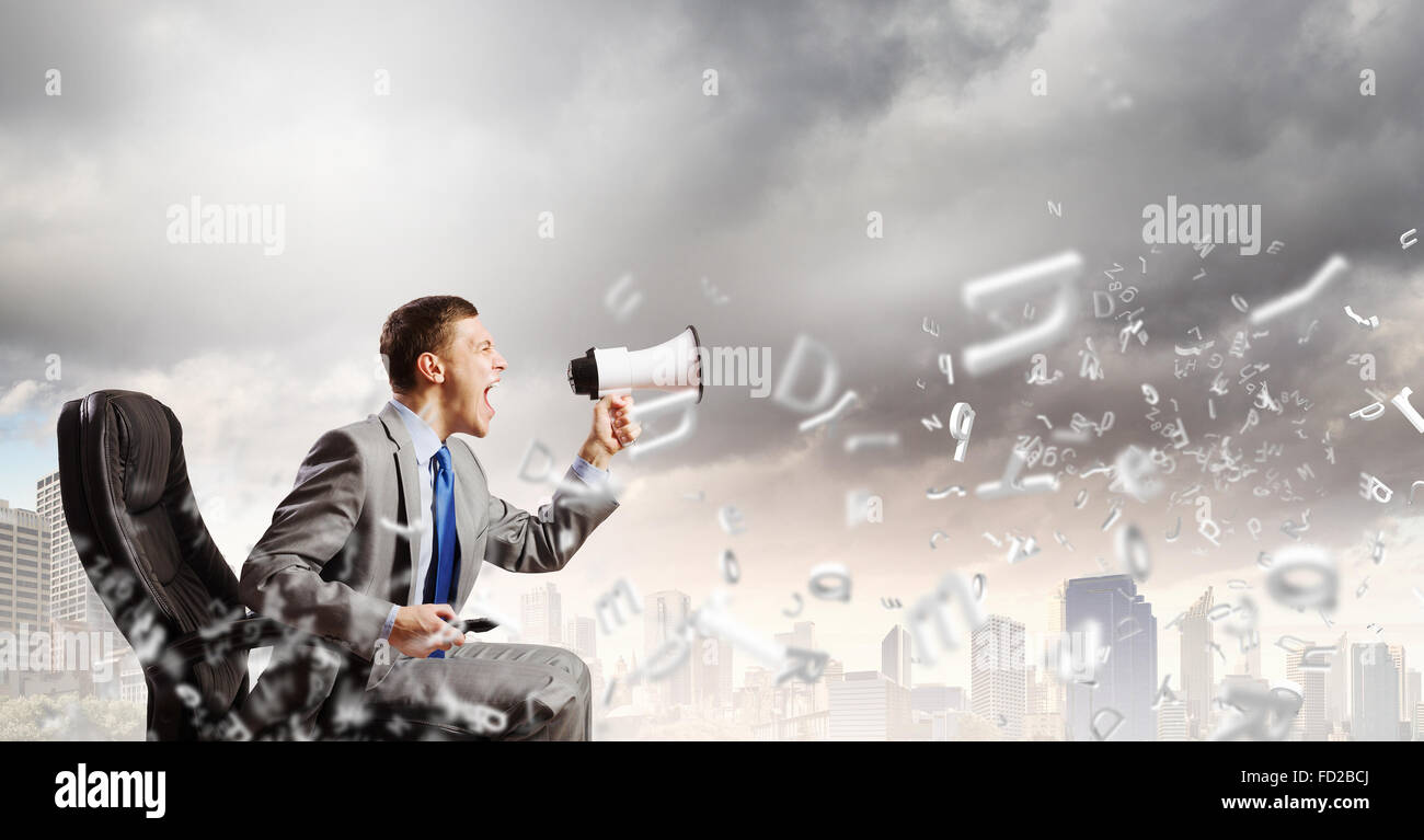 Young angry businessman sitting on chair and screaming in megaphone ...