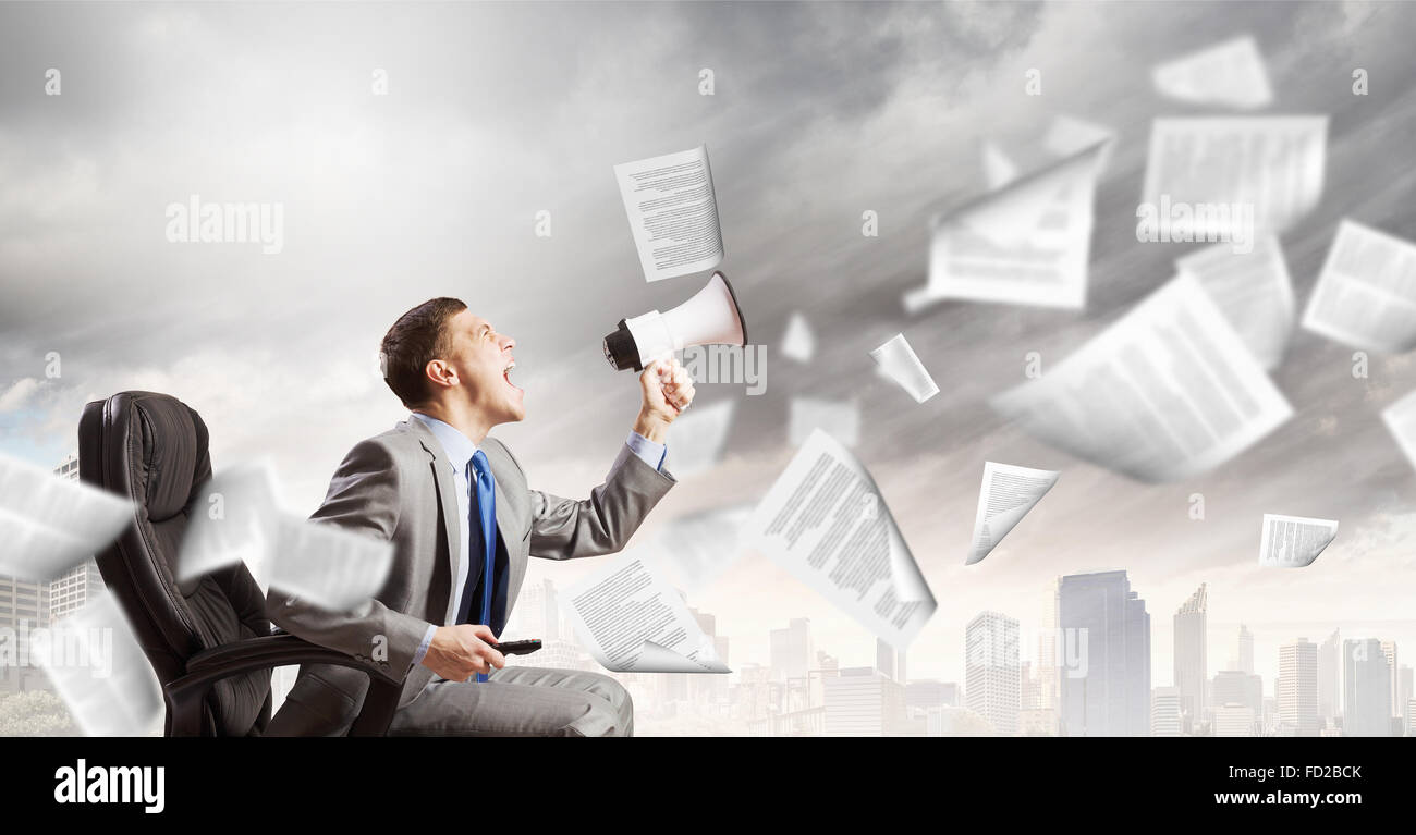 Young angry businessman sitting on chair and screaming in megaphone ...