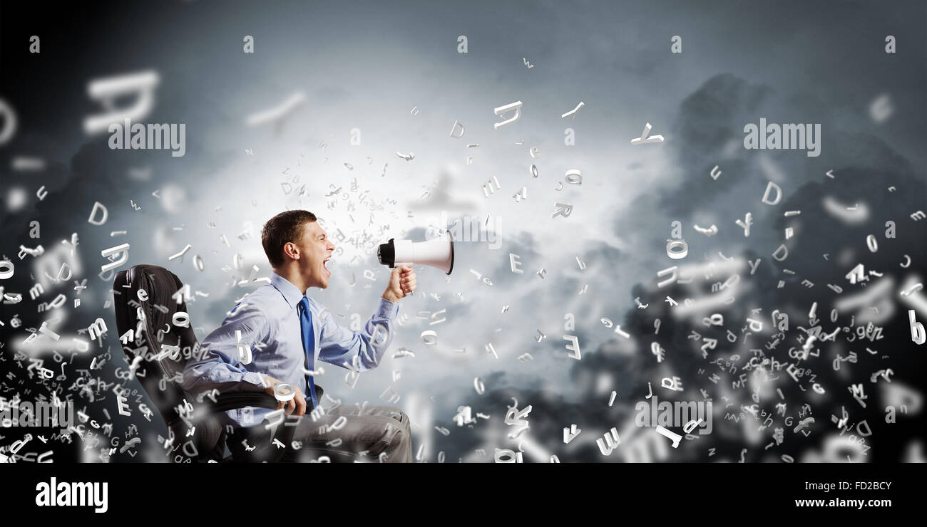 Young angry businessman sitting on chair and screaming in megaphone ...