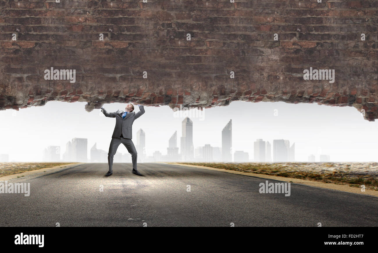 Young powerful businessman lifting brick wall above head Stock Photo ...