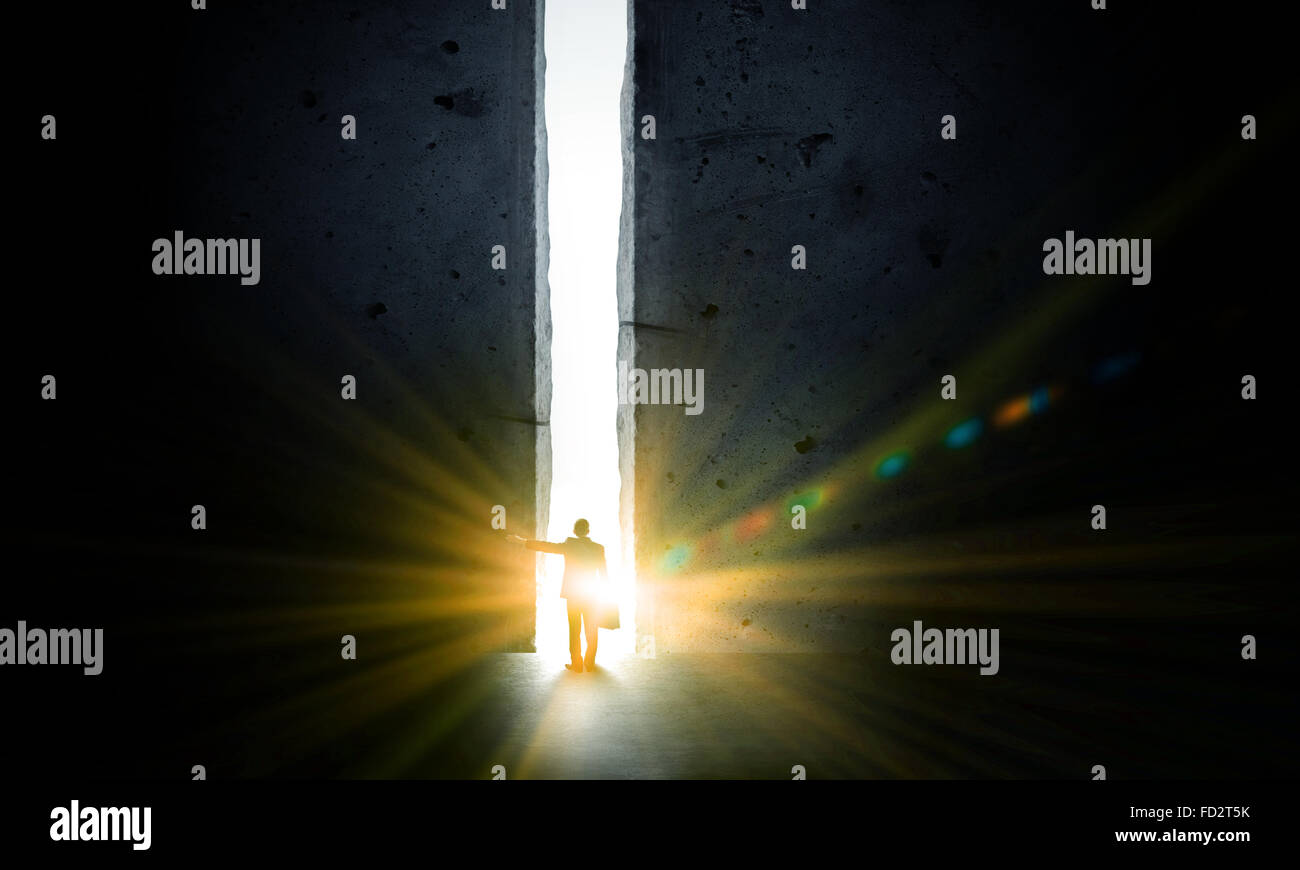 Rear view of businessman standing in light of way in wall Stock Photo ...
