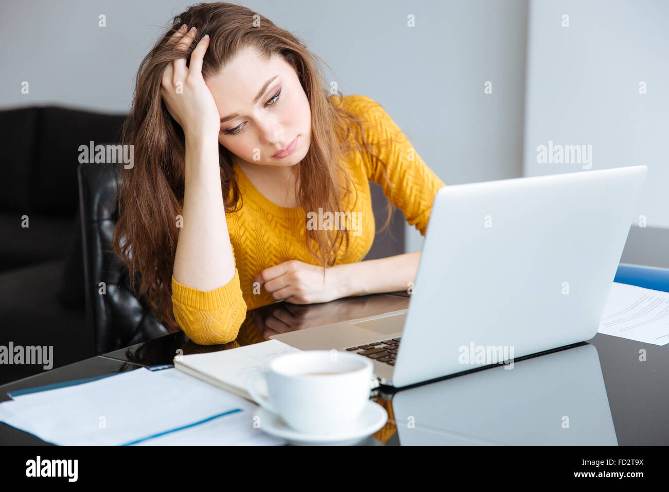 Sad woman sitting at the table with bills and laptop computer at home ...