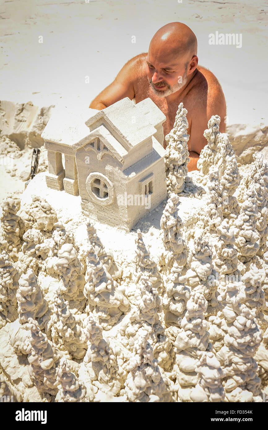 A man is surrounded by an elaborate sandcastle construction of trees ...