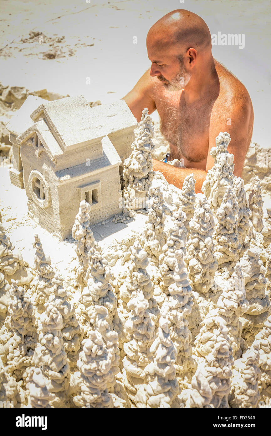 A man is surrounded by an elaborate sandcastle construction of trees ...