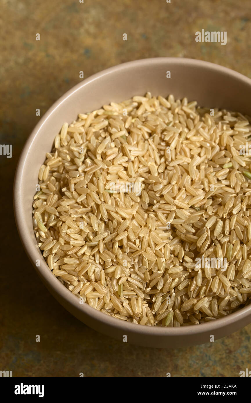 Raw brown or wholegrain rice kernels in bowl, photographed on slate ...