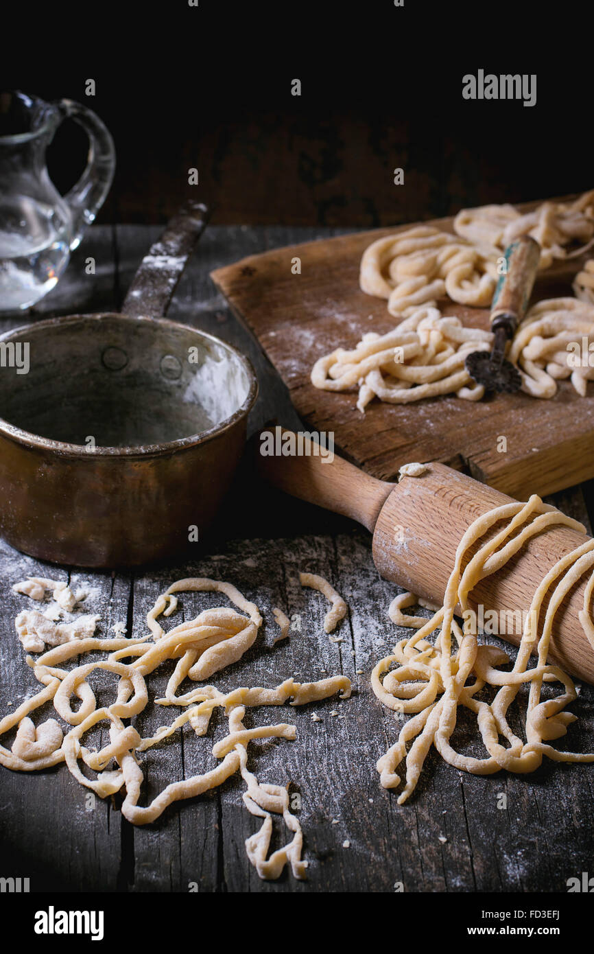 Fresh homemade pici pasta on wood chopping board over old wooden table ...
