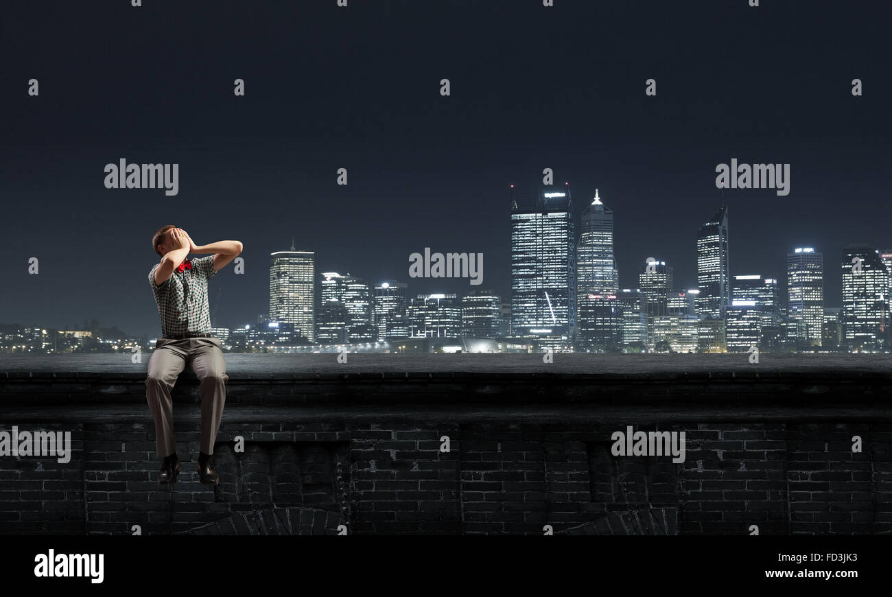 Young man sitting on building top and covering eyes with hands Stock ...