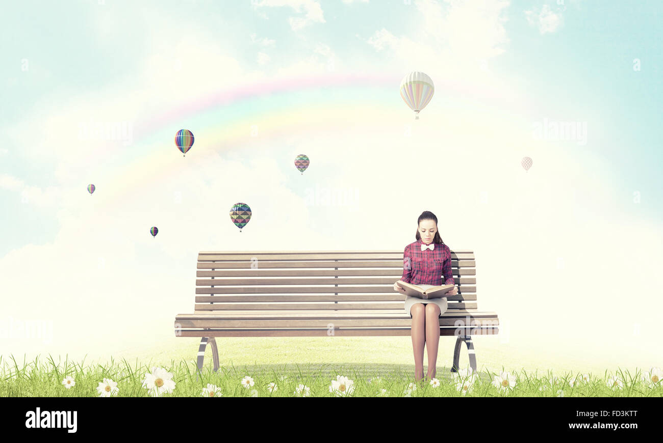 Young woman sitting on bench and reading book Stock Photo - Alamy