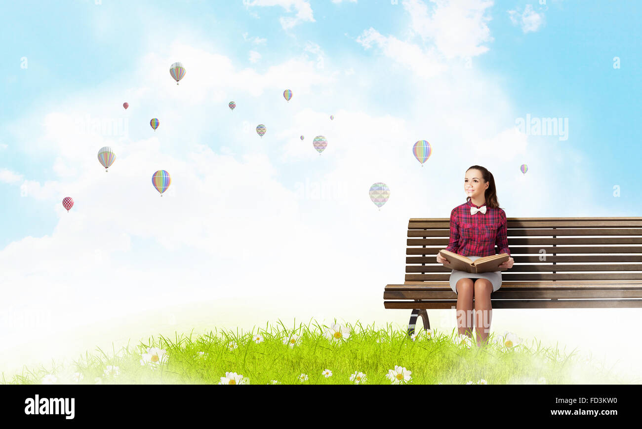 Young woman sitting on bench and reading book Stock Photo - Alamy
