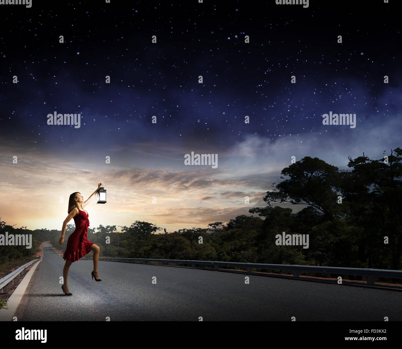 Young attractive woman in red dress with lantern walking in darkness ...