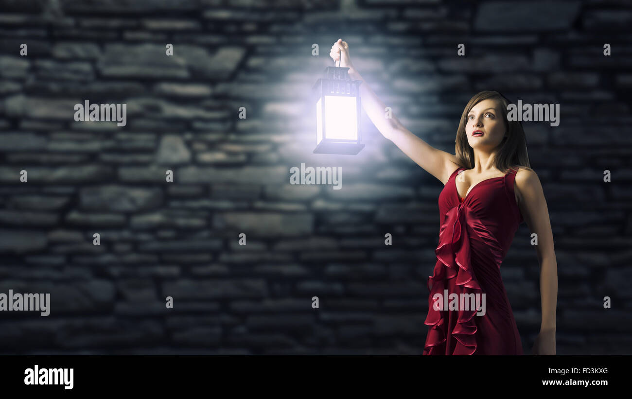 Young attractive woman in red dress with lantern walking in darkness ...